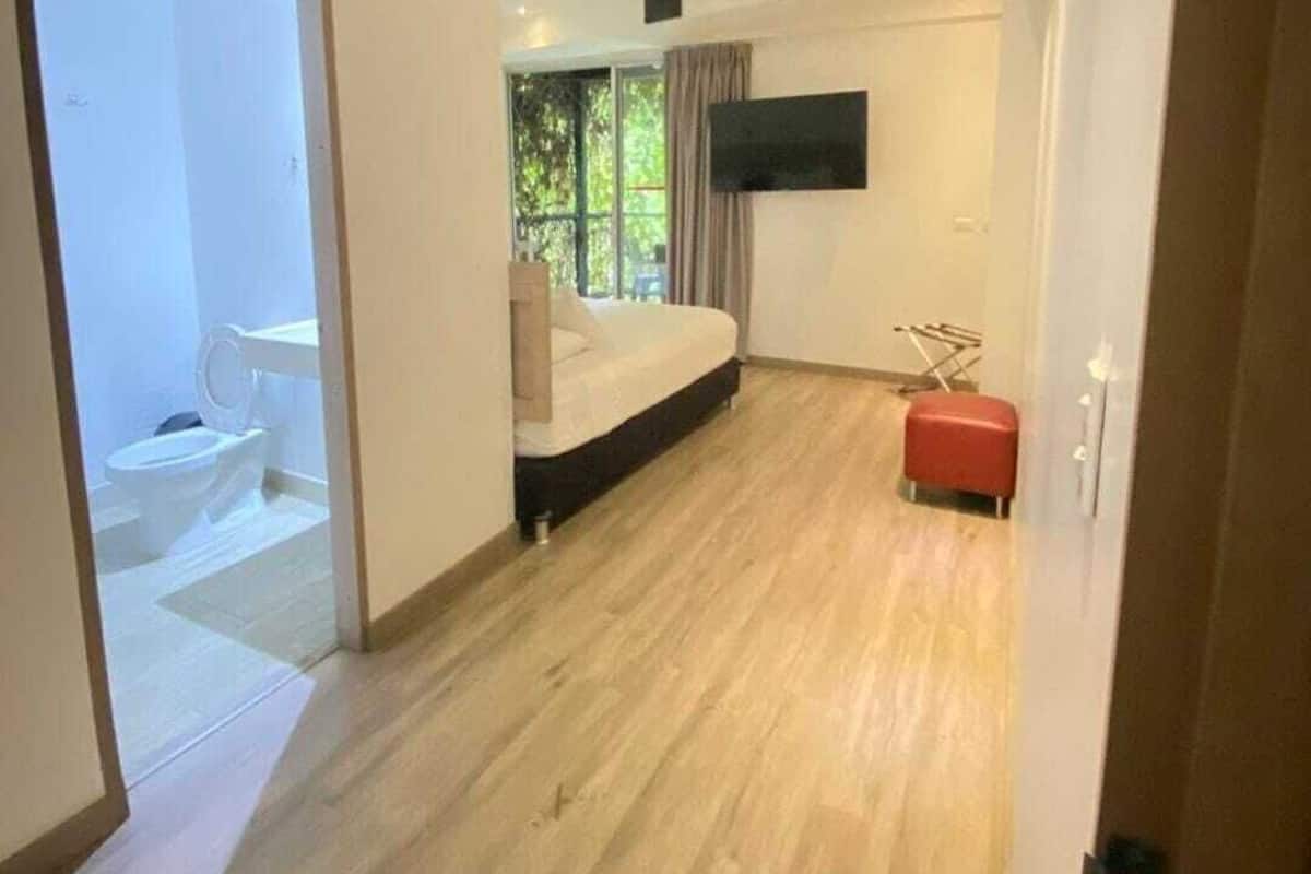 Quarto moderno com cama, televisão na parede e vista para o exterior através de uma janela.