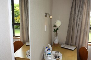 Quarto com mesa de madeira, um vaso com uma flor branca, garrafa de água, copo, lenço de papel e uma pequena bandeja com um caderno e caneta.
