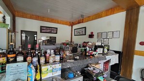 Uma área de bar com balcão, diversos tipos de garrafas e um letreiro com o cardápio.
