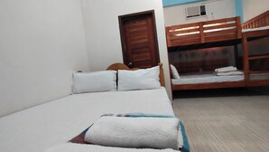 Uma cama de solteiro com roupa de cama e almofadas brancas, uma porta de madeira e uma cama beliche ao fundo.