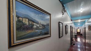 Um corredor com uma grande pintura emoldurada retratando uma paisagem ribeirinha, piso vermelho polido e teto azul.