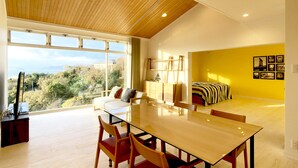 Uma sala de estar moderna com uma grande mesa de jantar de madeira, um sofá e uma cama com colcha listrada.