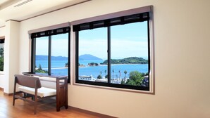 Quarto com uma grande janela que oferece vista para a praia e montanhas.