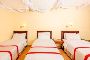 Quarto de hotel com duas camas de solteiro, cada uma com cabeceira de madeira, roupa de cama branca e detalhes vermelhos. Há mesas de cabeceira com abajures e um telefone.