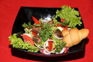 Salada com alface, tomate, cebola e um pão num bowl preto.