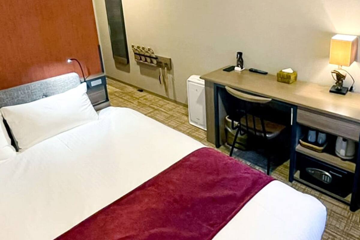 Quarto de hotel com cama, escrivaninha, cadeira, luminária e máquina de café.