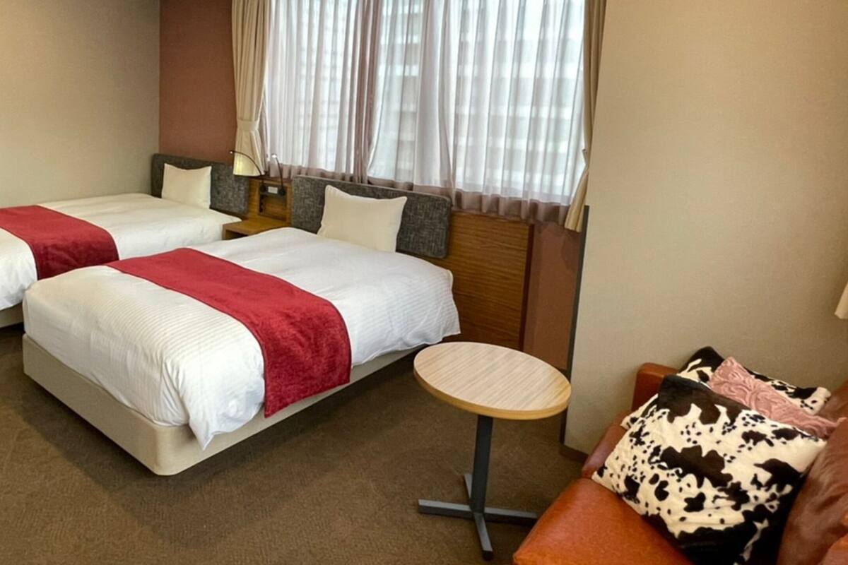 Quarto de hotel com duas camas, uma mesinha redonda e um sofá.