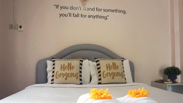 Uma cama bem arrumada com almofadas listradas e uma frase na parede.