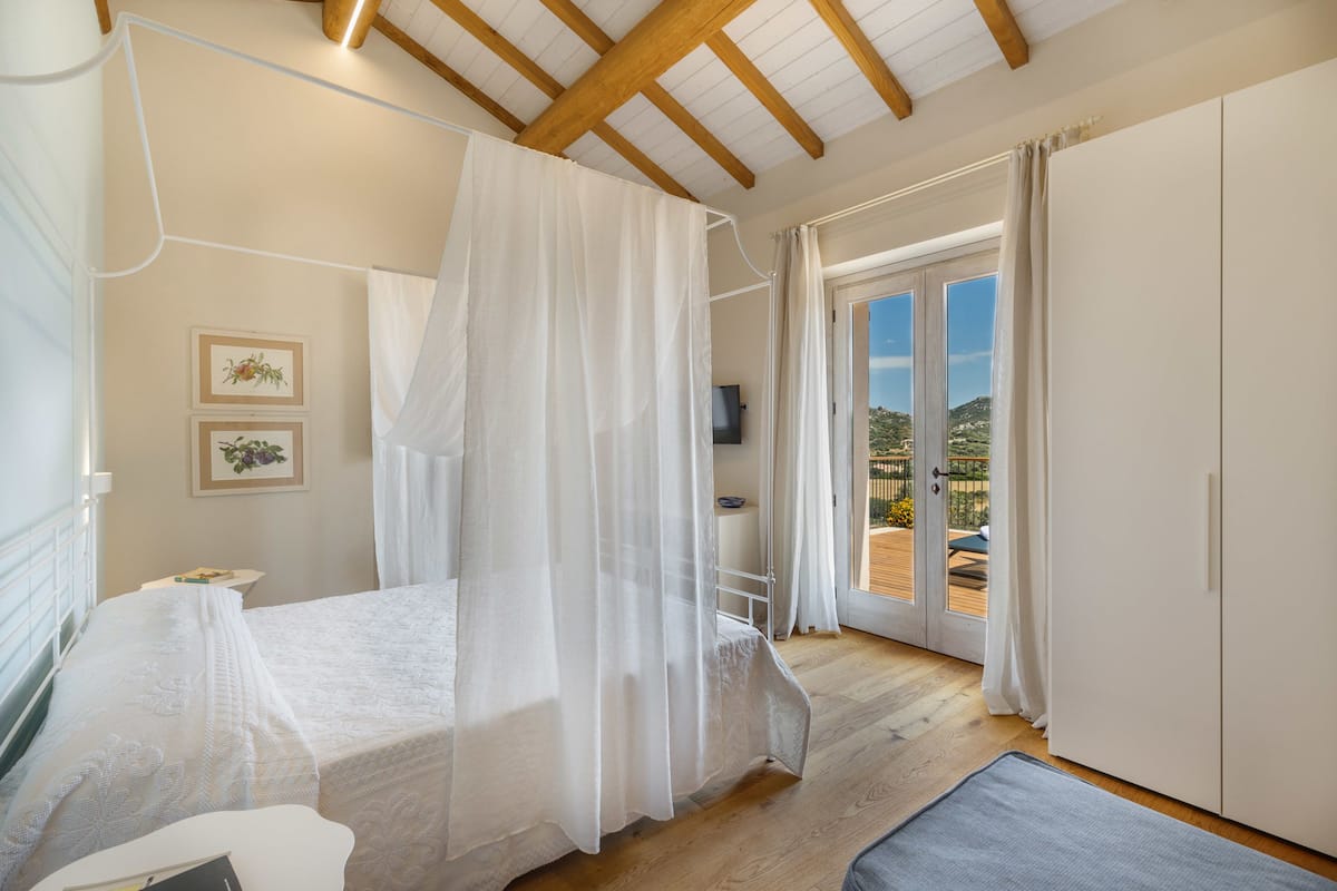 Quarto com cama, guarda-roupa, mesa de cabeceira, televisão e vista para o exterior.