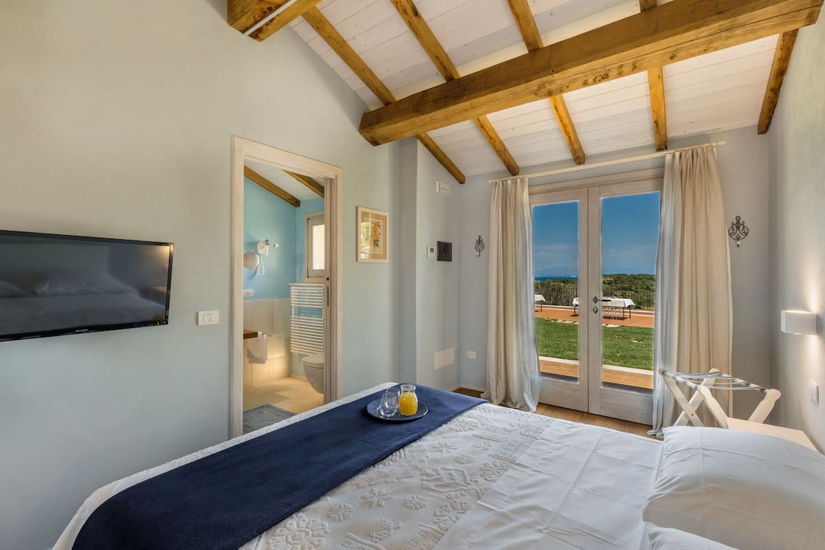 Quarto com cama, televisão, janela com cortinas e vista para o exterior.