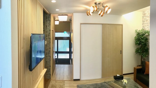 Uma sala de estar moderna com uma televisão de tela plana na parede, uma mesa de centro de vidro, uma planta em vaso e um guarda-roupa com porta deslizante.