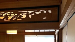 Quarto japonês tradicional com tatames, cama, cadeira e vista para o exterior.