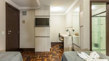 Quarto de hotel com duas camas, uma escrivaninha, um espelho, chuveiro e piso estampado.