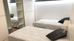 Quarto com duas camas, um guarda-roupa e uma luminária de cabeceira.
