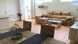 Uma sala de estar moderna com um sofá bege, uma mesa de jantar com uma cadeira de fibra natural e uma pequena mesa de centro.
