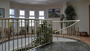 Interior espaçoso com escadaria em curva, grandes janelas e um espaço central com plantas.