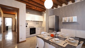 Cozinha moderna com armários brancos, geladeira de aço inoxidável e área de refeições com cadeiras brancas e mesa posta para quatro pessoas.
