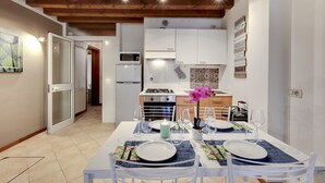 Uma área de refeições com uma mesa posta para dois, cozinha ao fundo e teto de madeira.