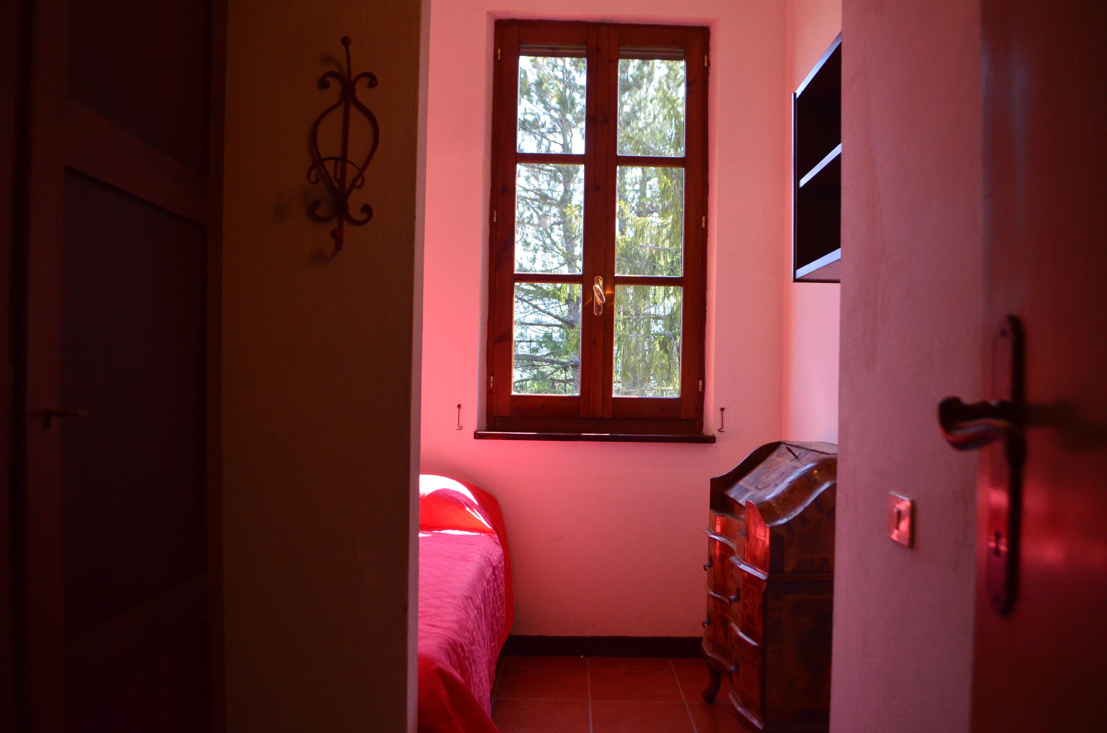 Um quarto com cama, penteadeira, janela com vista para árvores e porta.