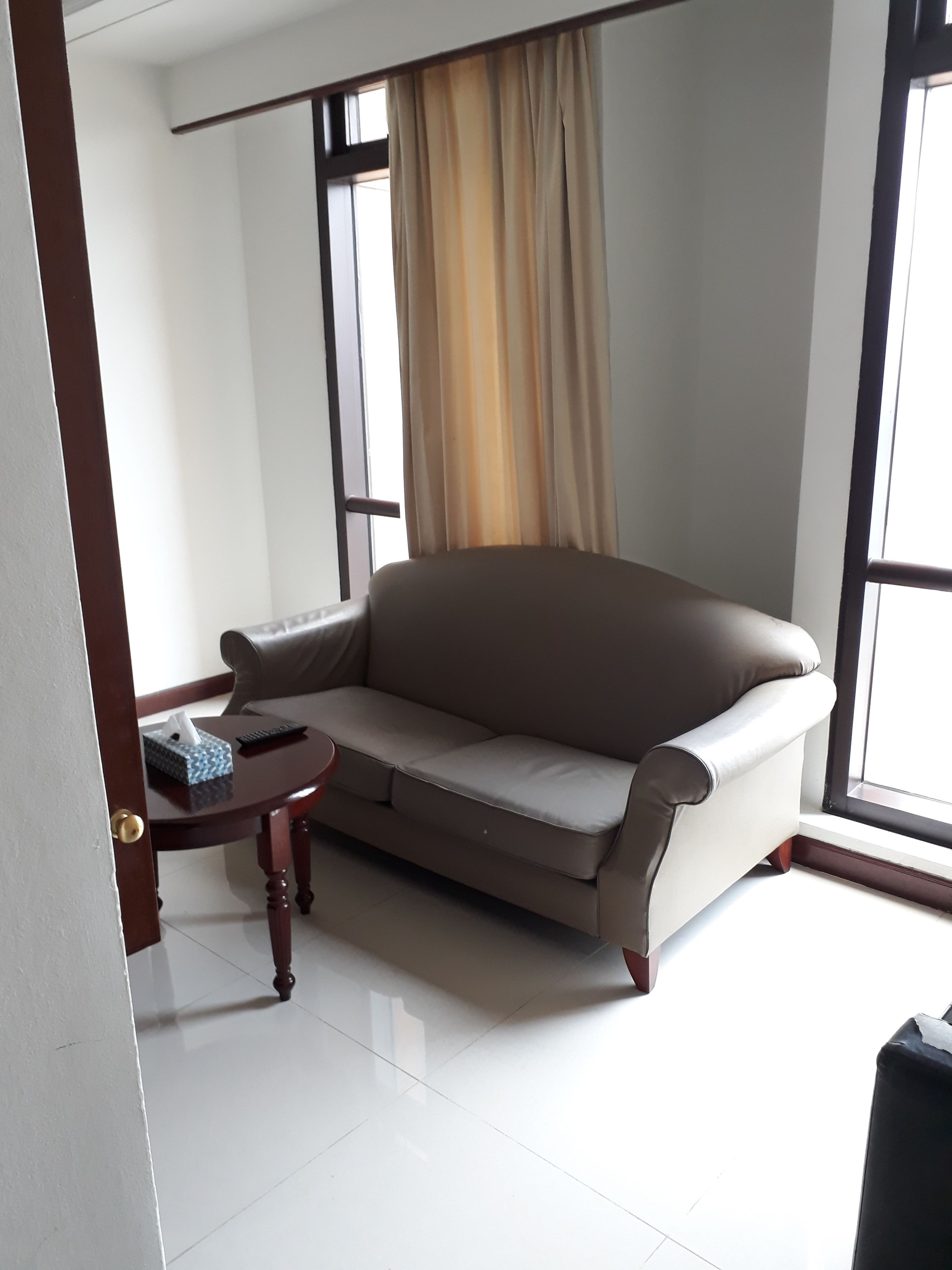 Uma sala de estar com um sofá, uma mesa pequena e uma janela com cortinas.