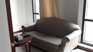 Uma sala de estar com um sofá, uma mesa pequena e uma janela com cortinas.