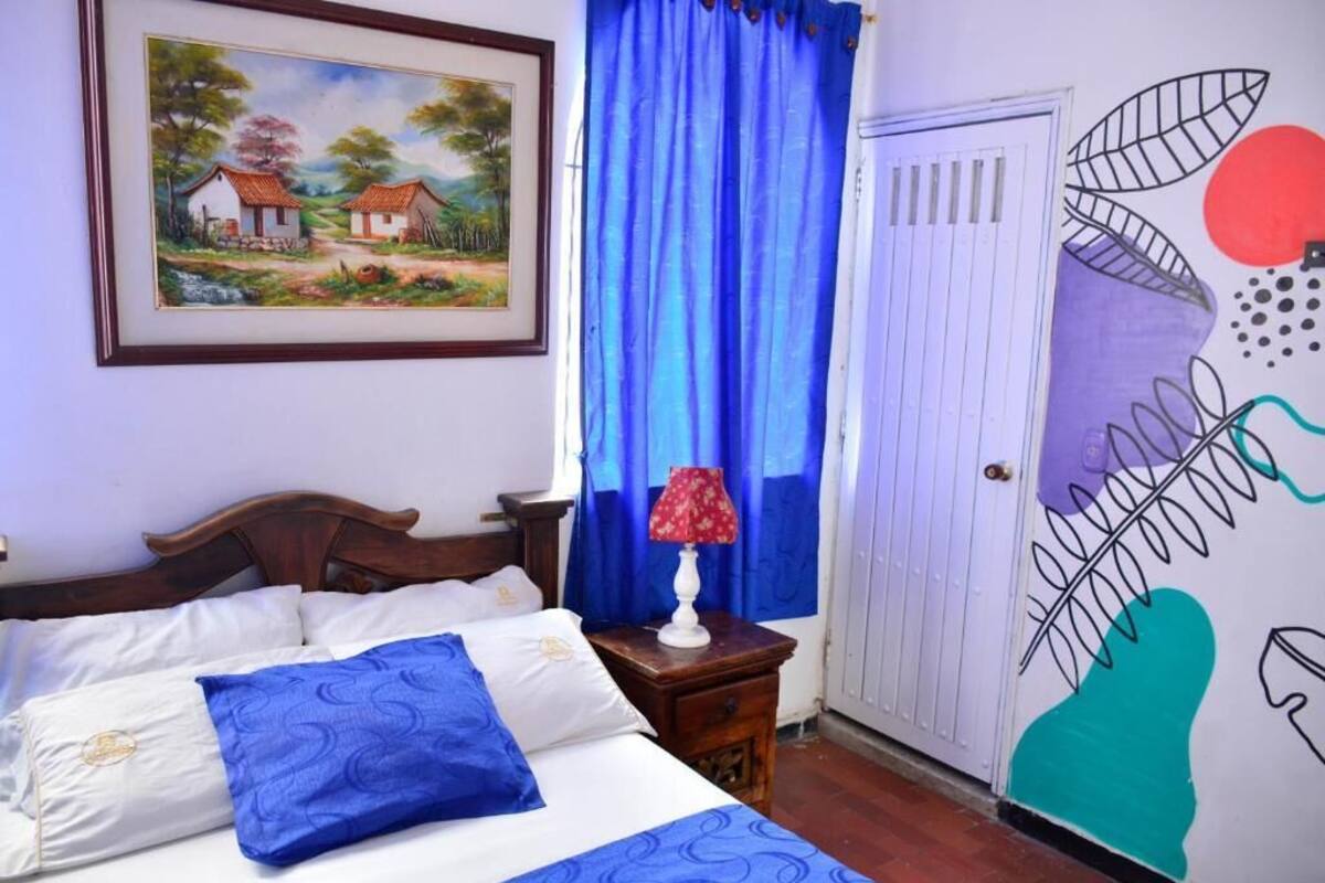 Quarto com cama, mesa de cabeceira, luminária, porta e pintura na parede.