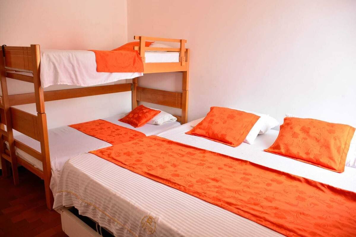 Quarto com beliche, duas camas com roupa de cama e almofadas laranja.