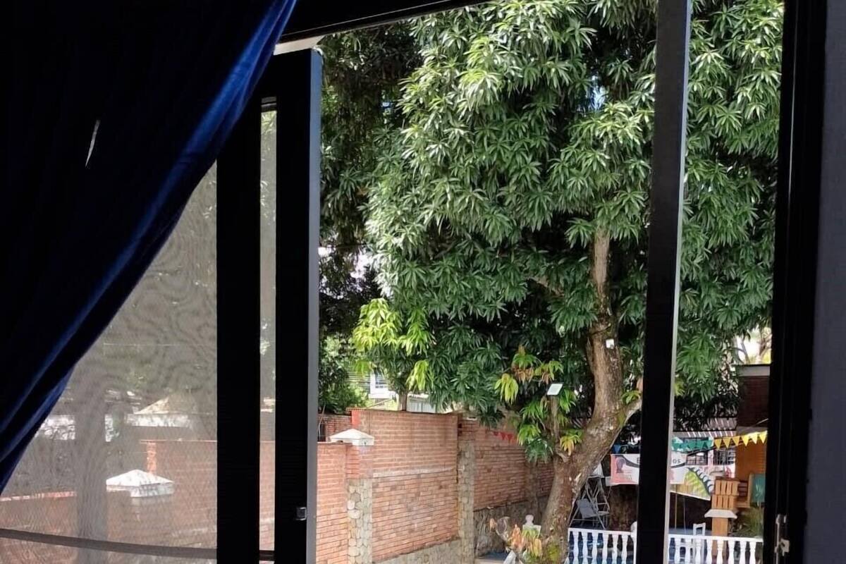 Vista de um quarto com porta de vidro que se abre para área externa com piscina, muro de tijolos e uma árvore.
