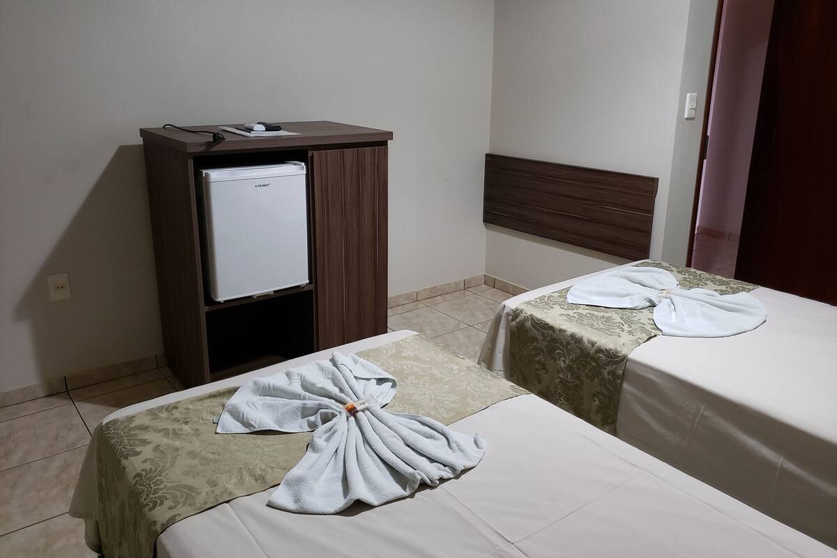 Quarto de hotel com duas camas, um minibar e uma cabeceira de madeira.