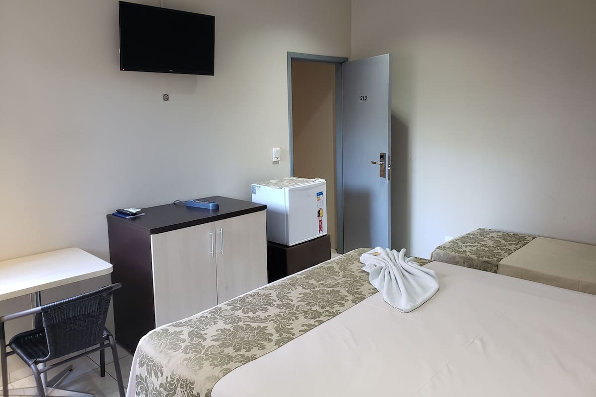 Quarto de hotel com cama, escrivaninha, cadeira, televisão, minibar e armário.