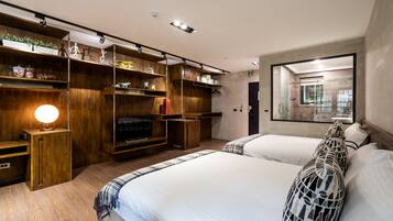 Quarto de hotel com duas camas, estantes de madeira com diversos objetos, uma televisão e uma janela grande com vista para o exterior.