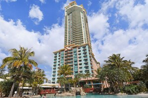 Um hotel alto com várias varandas, rodeado por palmeiras e uma piscina.