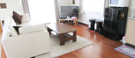 Uma sala de estar com sofá, mesa de centro, televisão e geladeira.