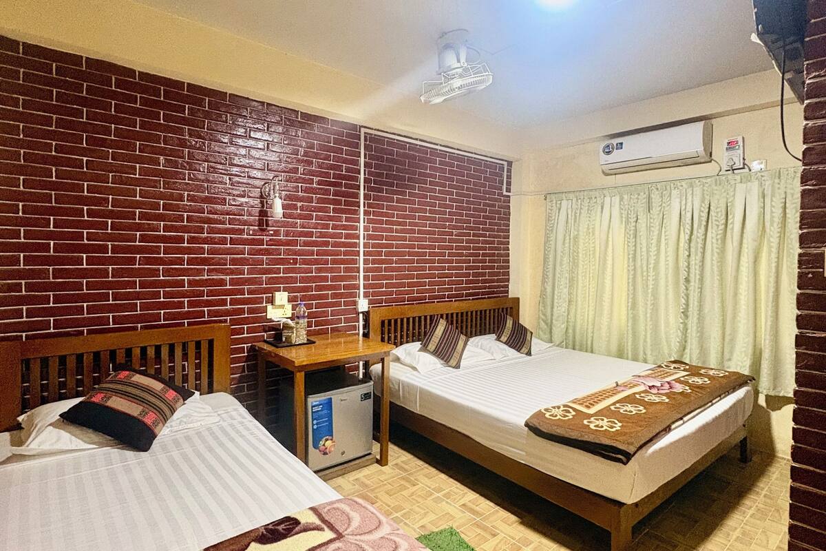 Quarto de hotel com duas camas, uma escrivaninha, um pequeno frigorífico e um ar condicionado.