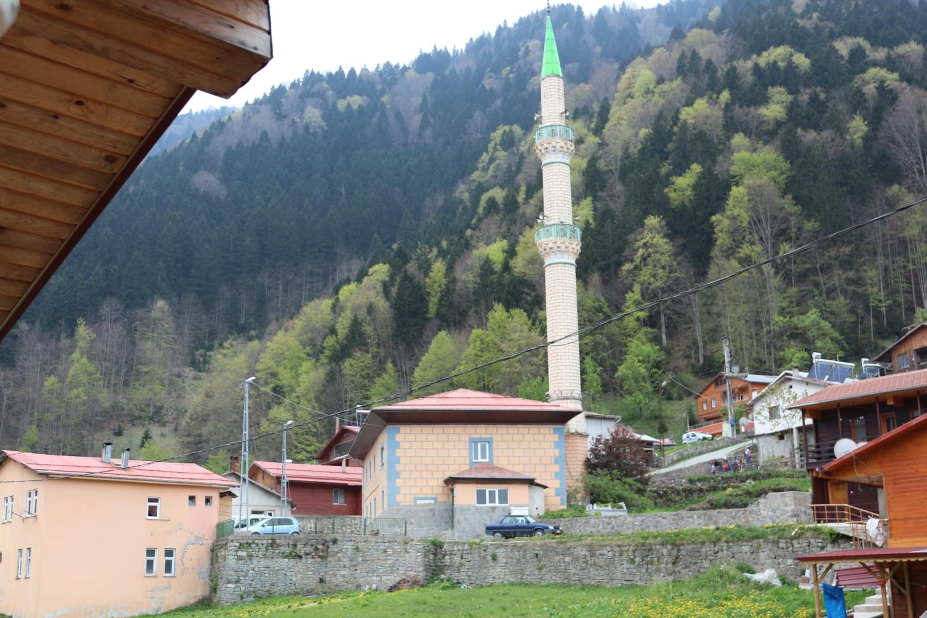 Um edifício tradicional com um minarete imponente, rodeado por casas residenciais e uma paisagem montanhosa ao fundo.