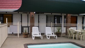 Uma área de piscina com duas espreguiçadeiras brancas e uma mesa, cercada por uma vedação branca.