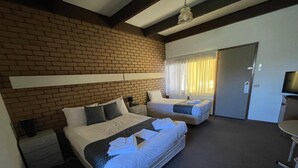 Quarto de hotel com parede de tijolos, duas camas, uma mesa e uma televisão.