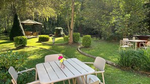 Um jardim com mesa e cadeiras, cercado por sebes e árvores bem aparadas.