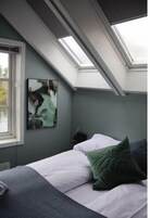 Quarto com claraboia, cama com almofadas e um quadro na parede.
