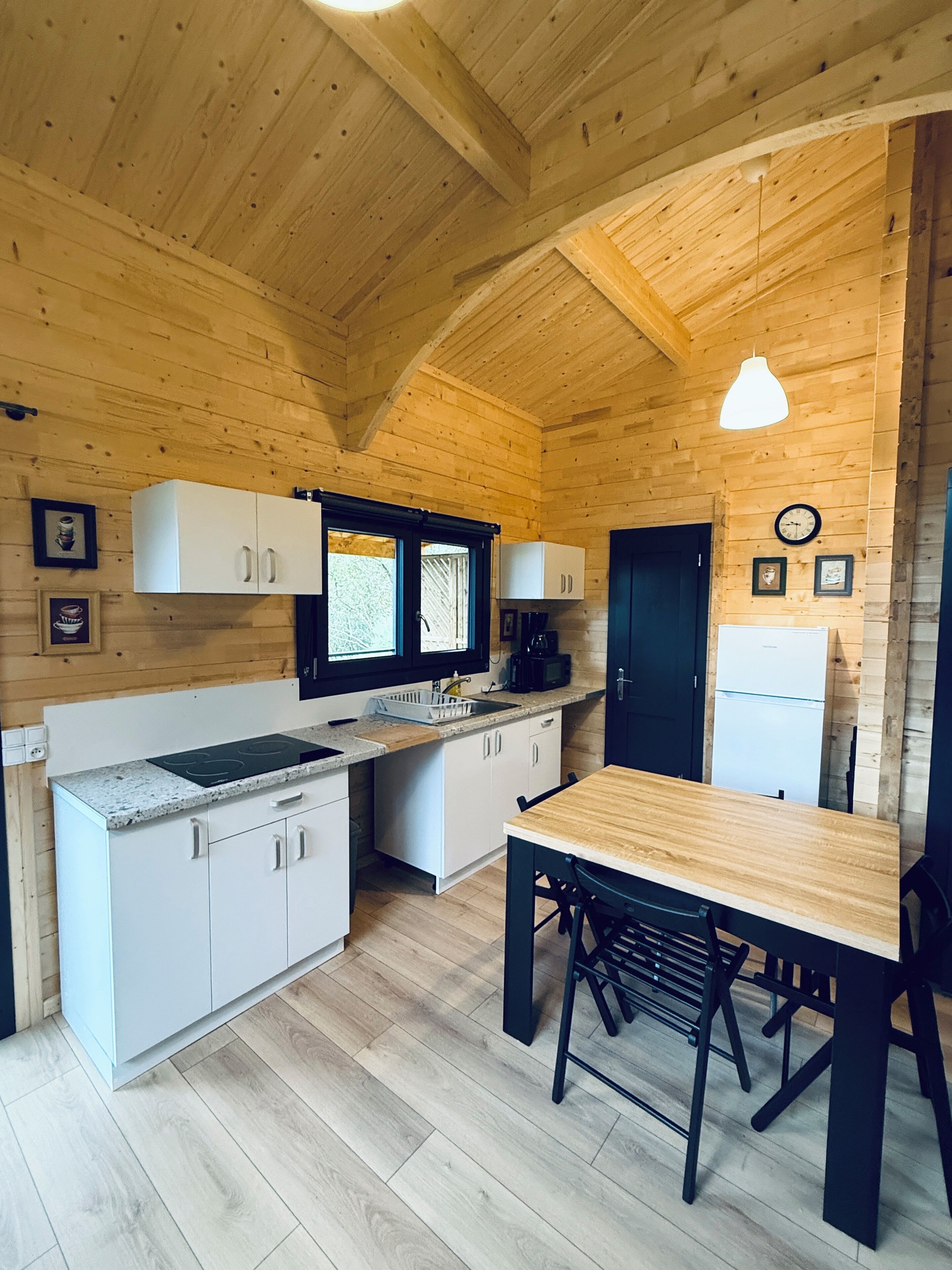 Uma cozinha compacta com armários brancos, uma mesa de madeira e uma porta com moldura preta.