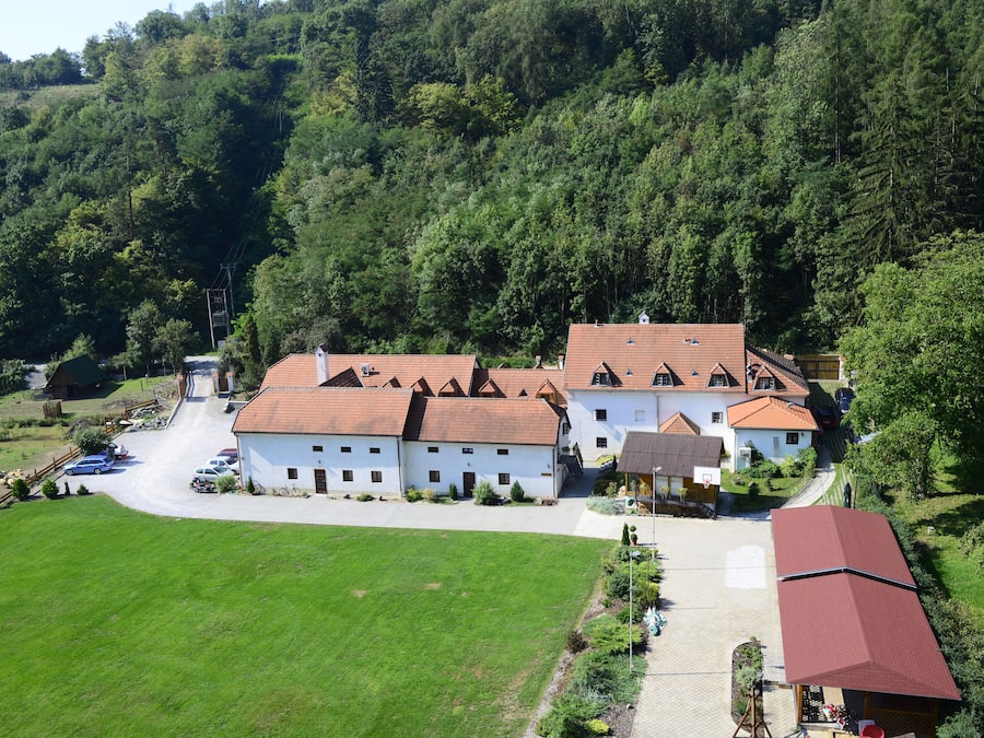 Um edifício grande e de vários andares com telhado de telhas vermelhas, cercado por vegetação exuberante e um gramado bem cuidado.