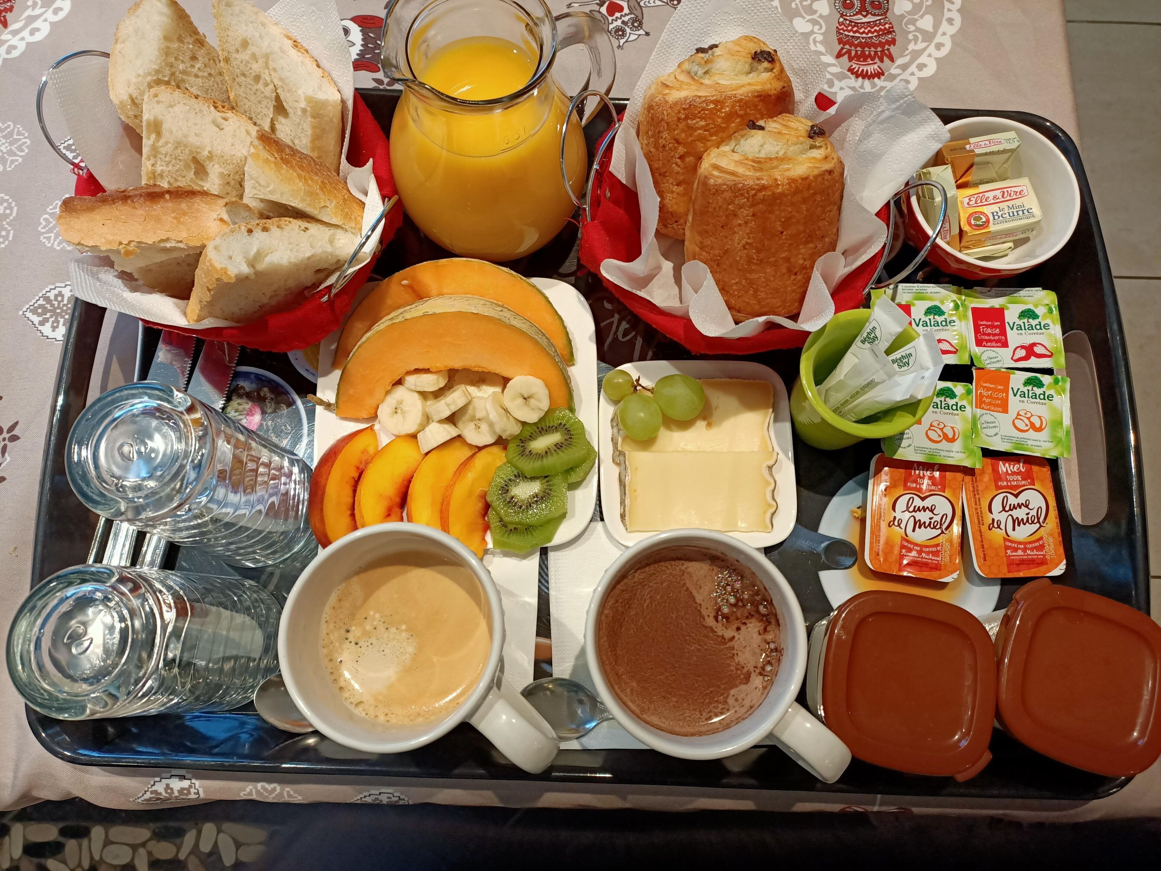 Uma bandeja de café da manhã com pão, suco de laranja, doces, frutas, queijo e lanches embalados.