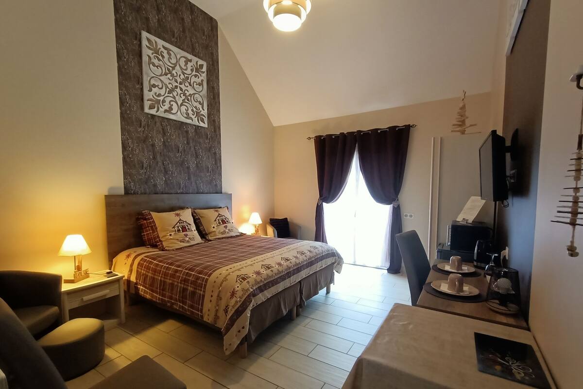 Quarto de hotel com cama, mesas de cabeceira, escrivaninha, cadeira, televisão e uma grande janela com cortinas.