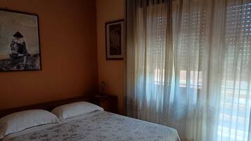 Quarto com cama, mesa de cabeceira, um quadro e cortinas finas.