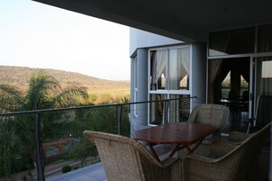 Uma varanda com cadeiras de vime e uma mesa, com vista para uma paisagem montanhosa.