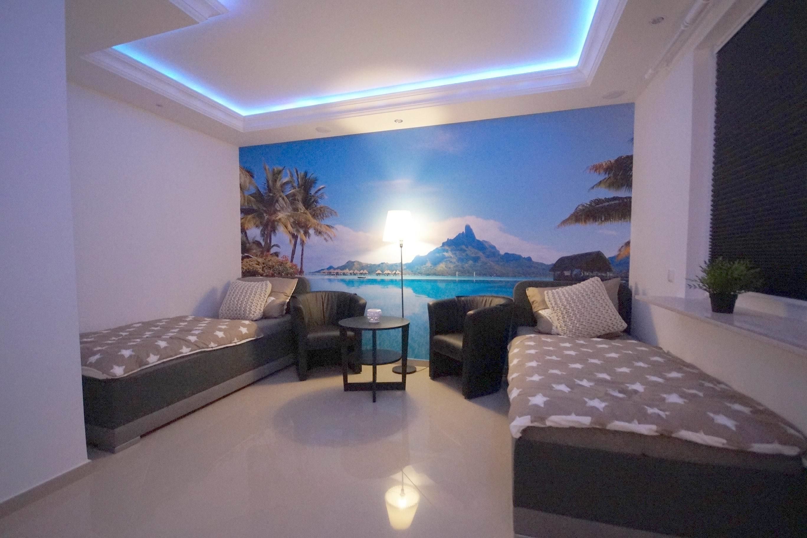 Quarto com uma cama, duas poltronas, uma mesinha e um mural com uma praia.