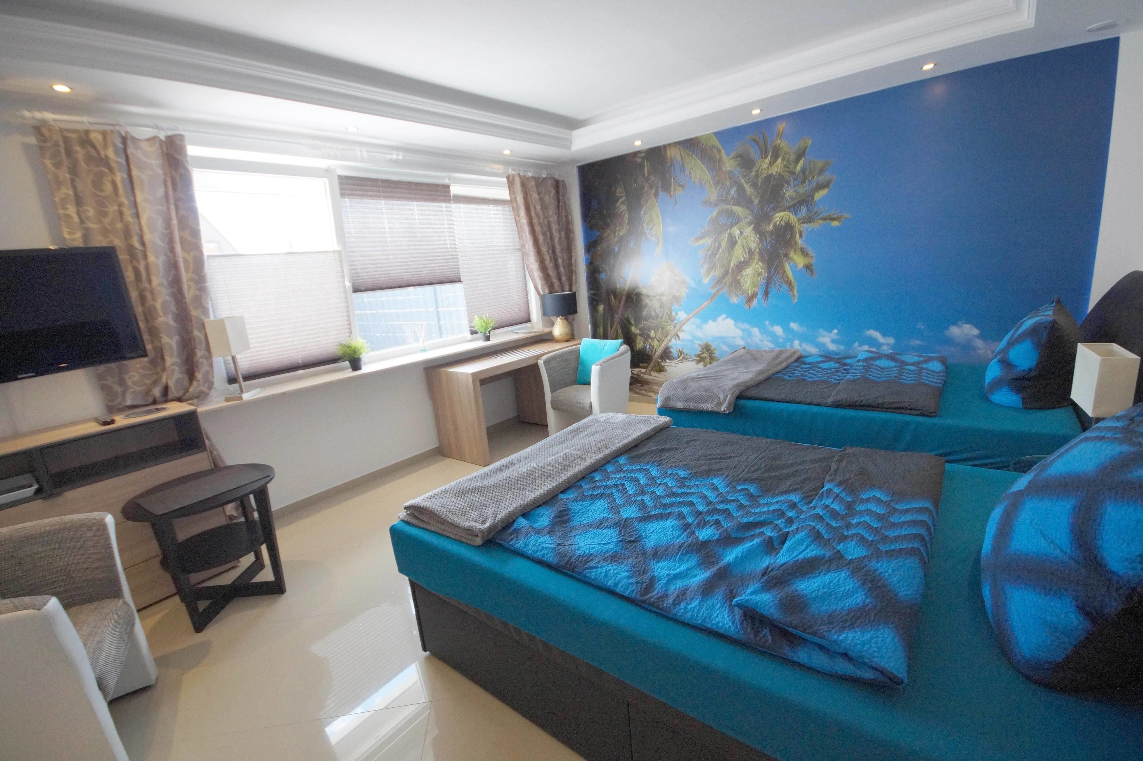 Quarto de hotel com duas camas, uma mesa, televisão e janela com cortinas.