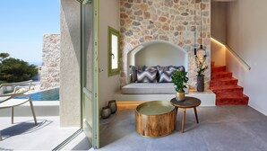 Um interior moderno com parede de pedra, um sofá com almofadas estampadas, uma mesa de madeira e uma escada.