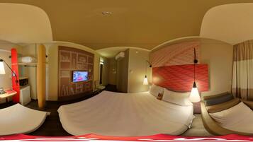 Quarto de hotel com cama, escrivaninha com abajur, televisão e parede com um padrão vermelho.