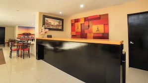 Uma área de recepção de hotel com um balcão preto, um quadro com uma vista da cidade e uma parede com padrão geométrico.